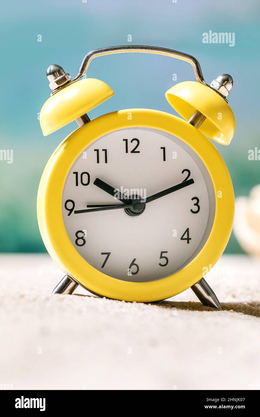 Close up of yellow alarm clock on summer sand sea beach with waves at ...