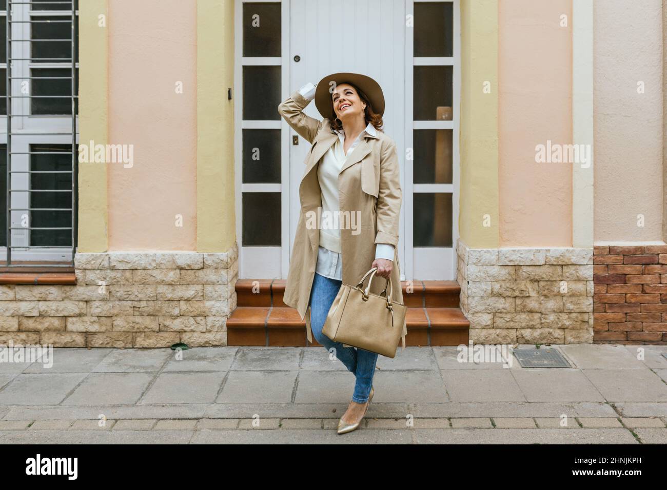 An adult woman in front of her front door posing with her hat and purse ...