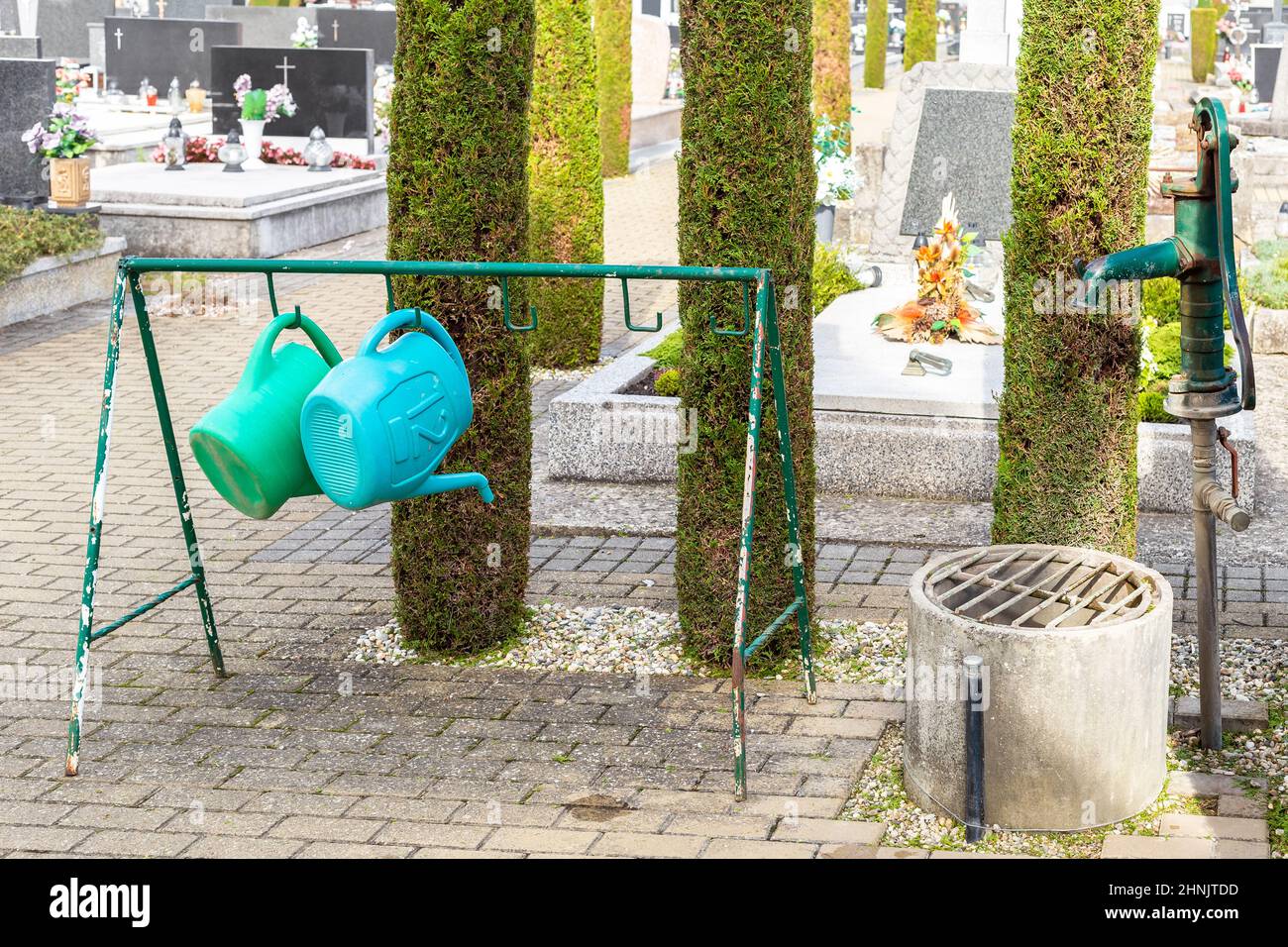 Watering cans hanging next to an old water pump at municipal cemetery ...