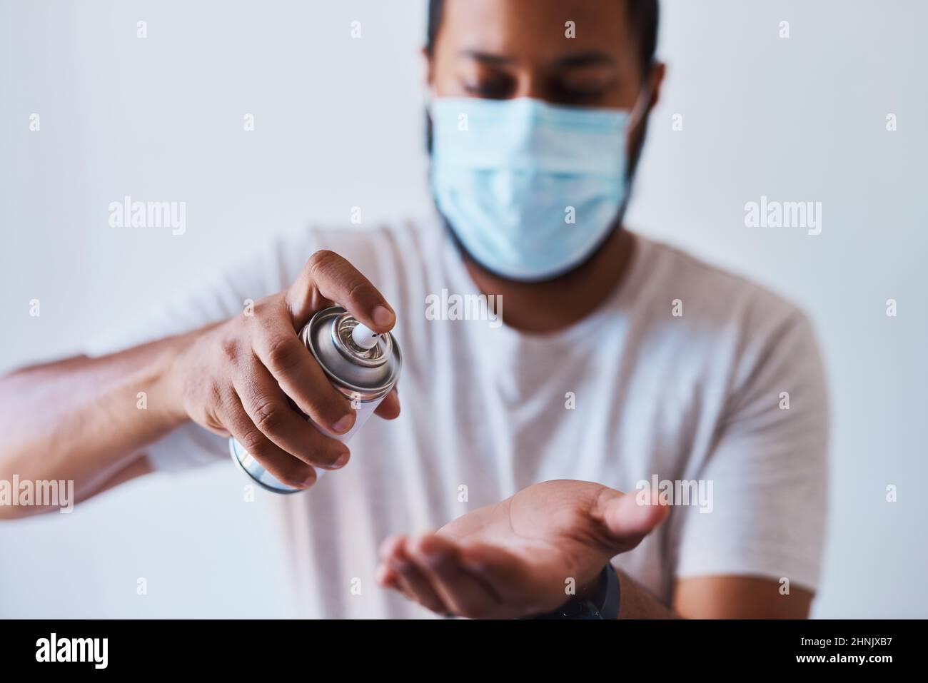 A close up shot of a young man spraying hand sanitiser onto his palm ...