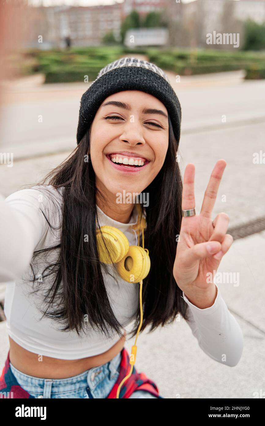 Selfie of a young latina while smiling and making the peace sign with ...