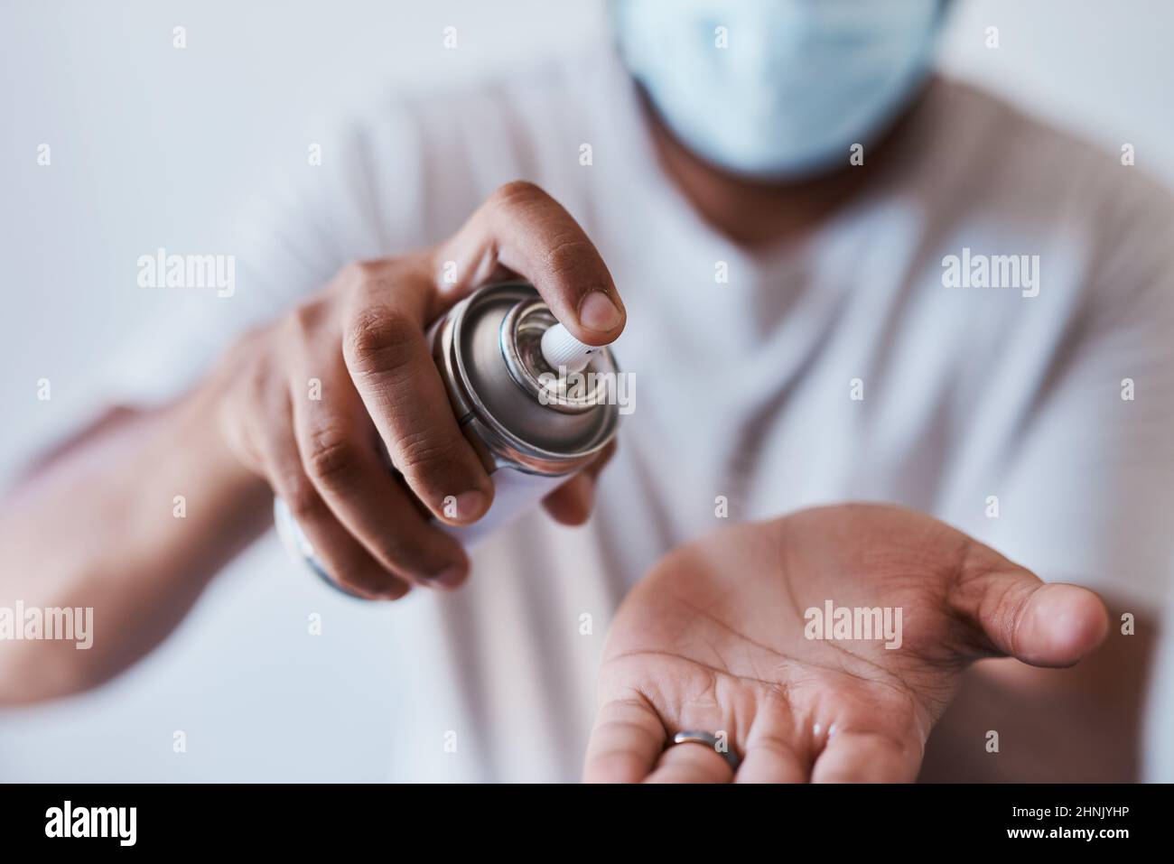 A close up shot of a young man spraying hand sanitiser onto his palm ...