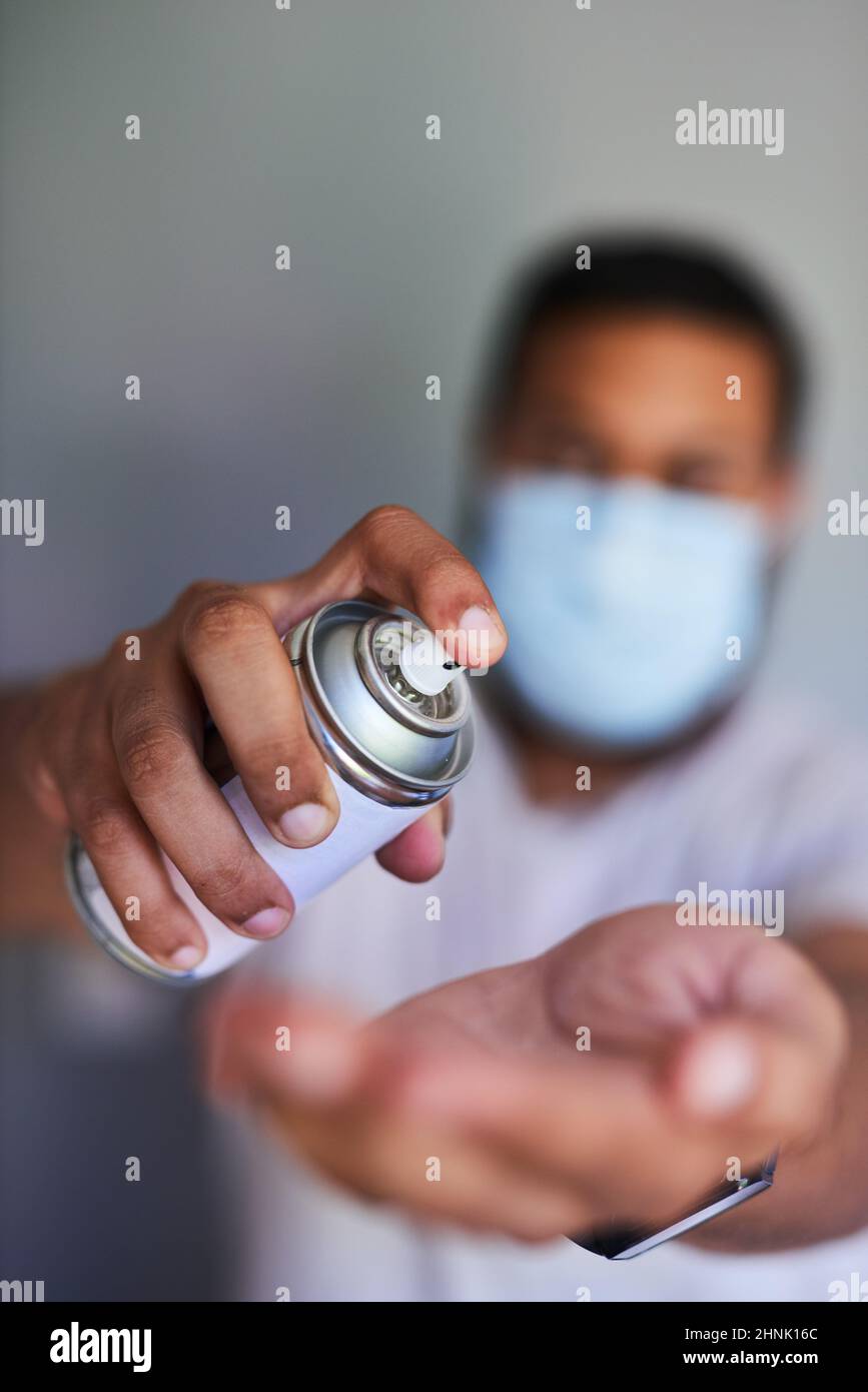 A close up shot of a young man spraying hand sanitiser onto his palm ...