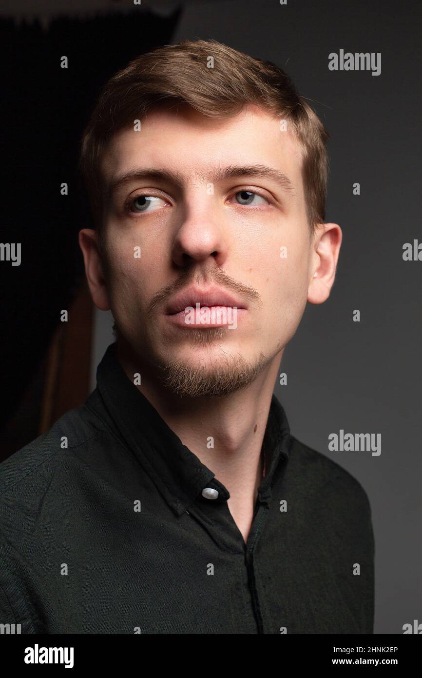 Young blond european man with short beard and mustache isolated on dark ...