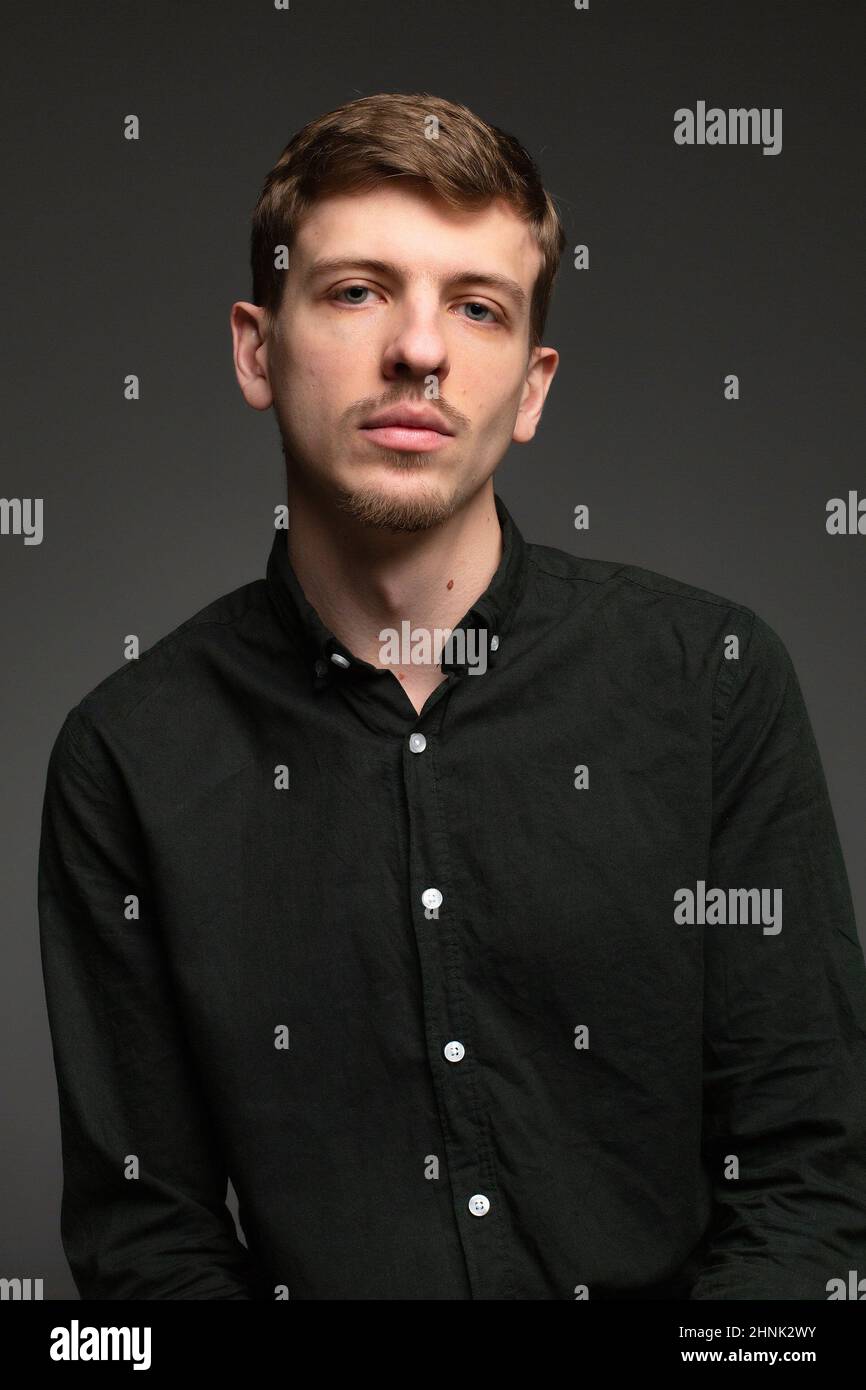 Young blond european man with short beard and mustache isolated on dark ...