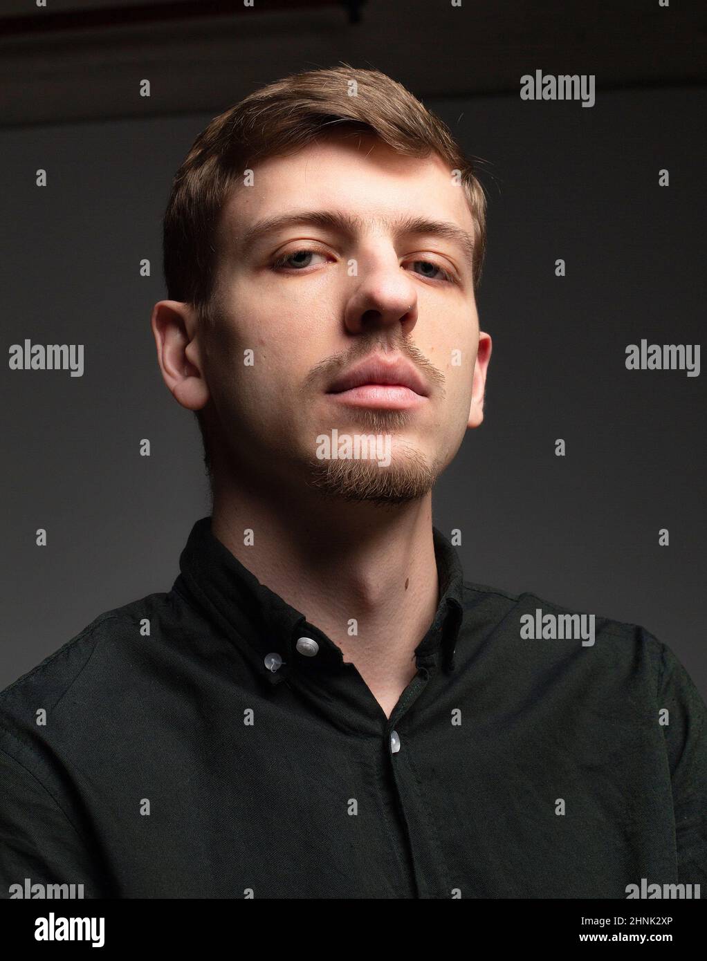 Young blond european man with short beard and mustache isolated on dark ...