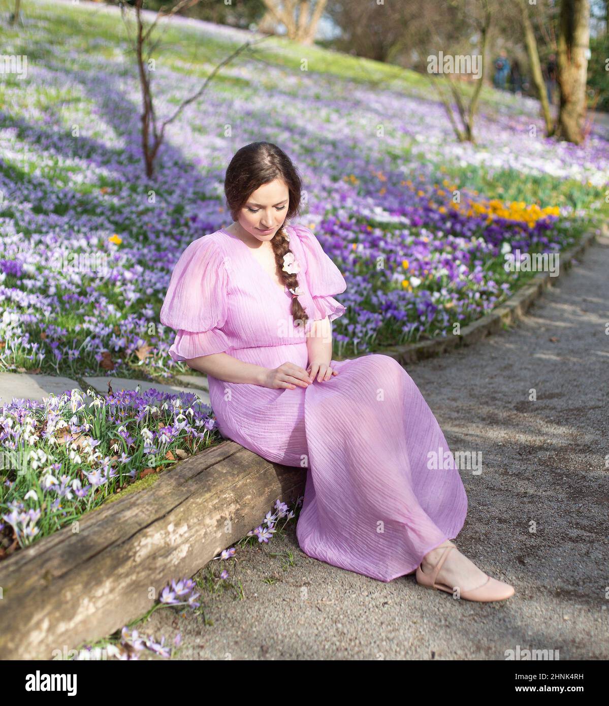 European woman in lilac dress with flowers in hair in park on a spring ...