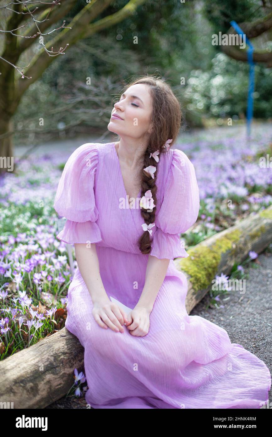 European woman in lilac dress sitting with brown hair in park with ...