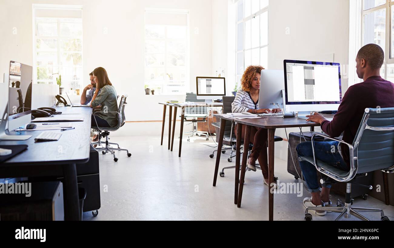 Working in an open plan office. Shot of colleagues working on their ...