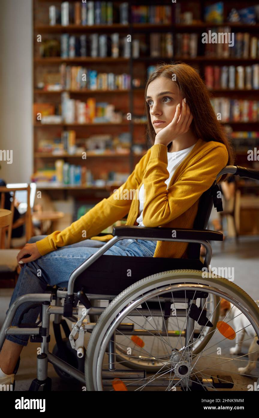 Thoughtful disabled female student in wheelchair, disability, bookshelf ...