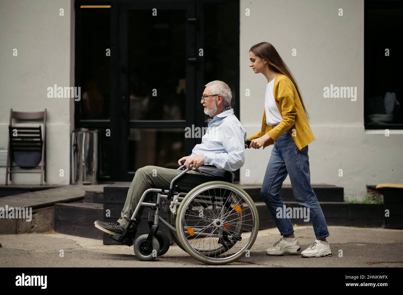 Daughter and disabled father in wheelchair go for a walk. Paralyzed ...