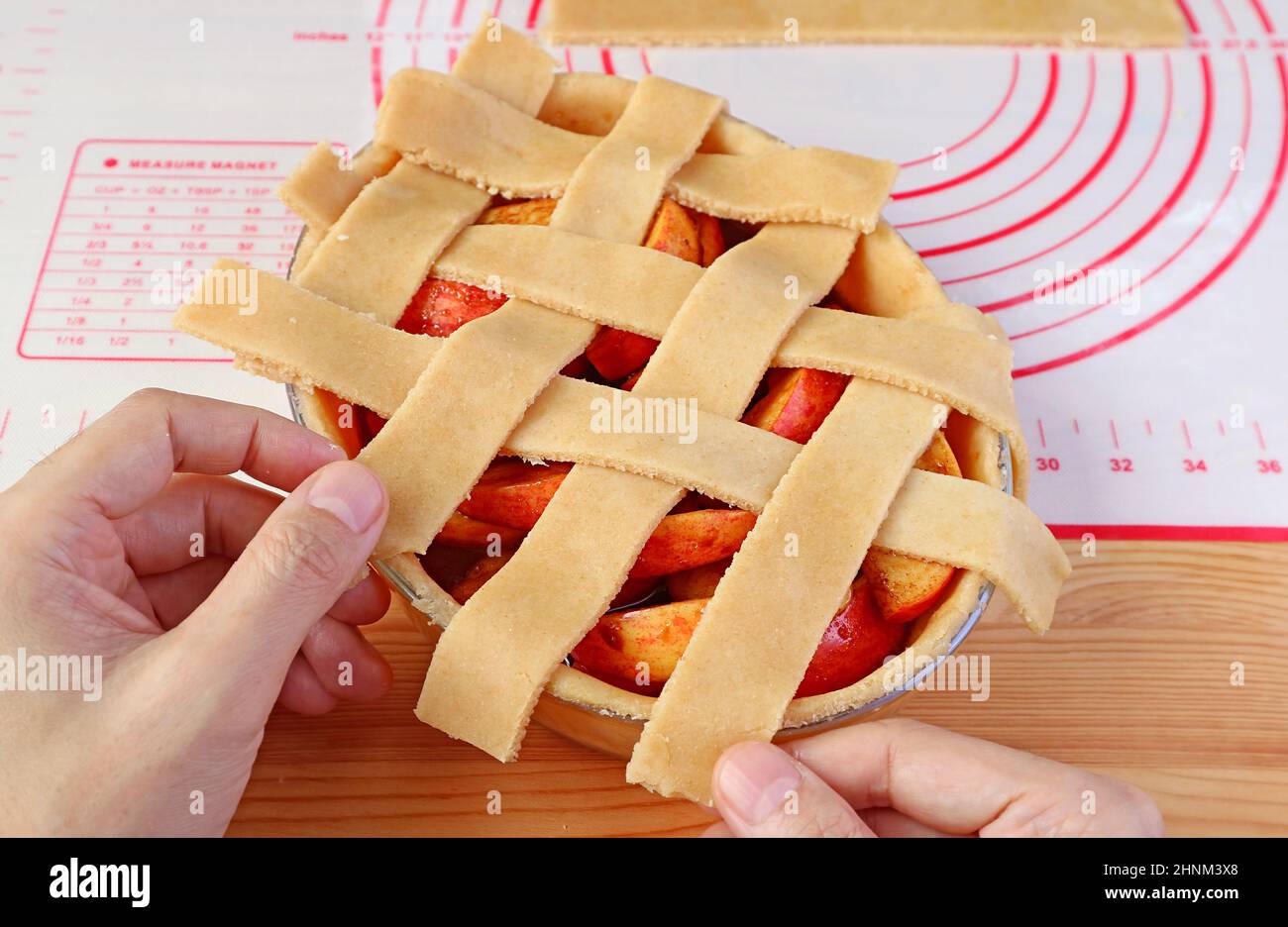 Hand weaving pieces of cut dough on pie plate for lattice top crust of ...