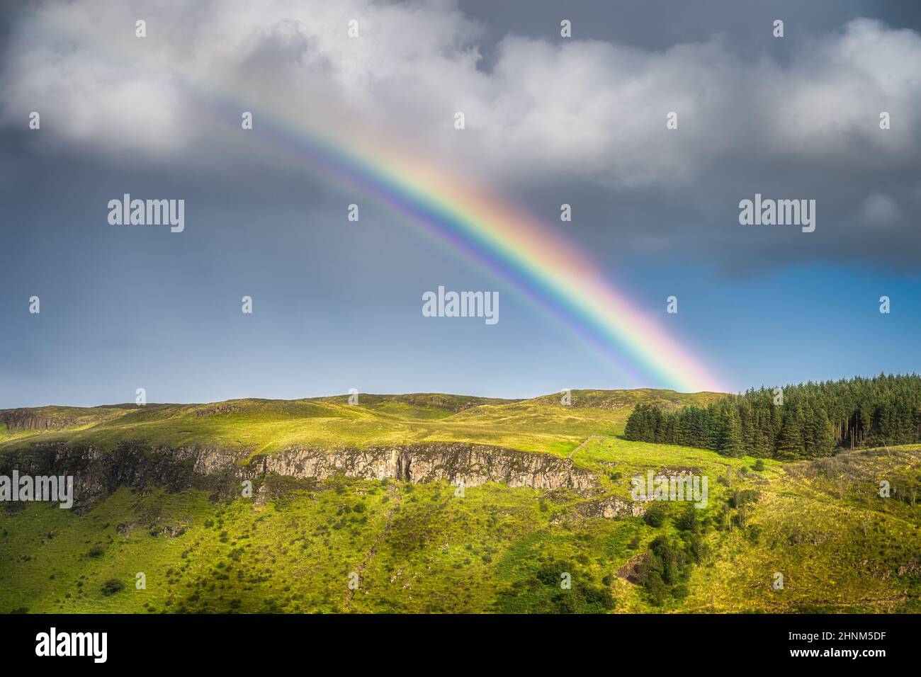 Closeup on vivid rainbow arching over hills and forests covered in ...