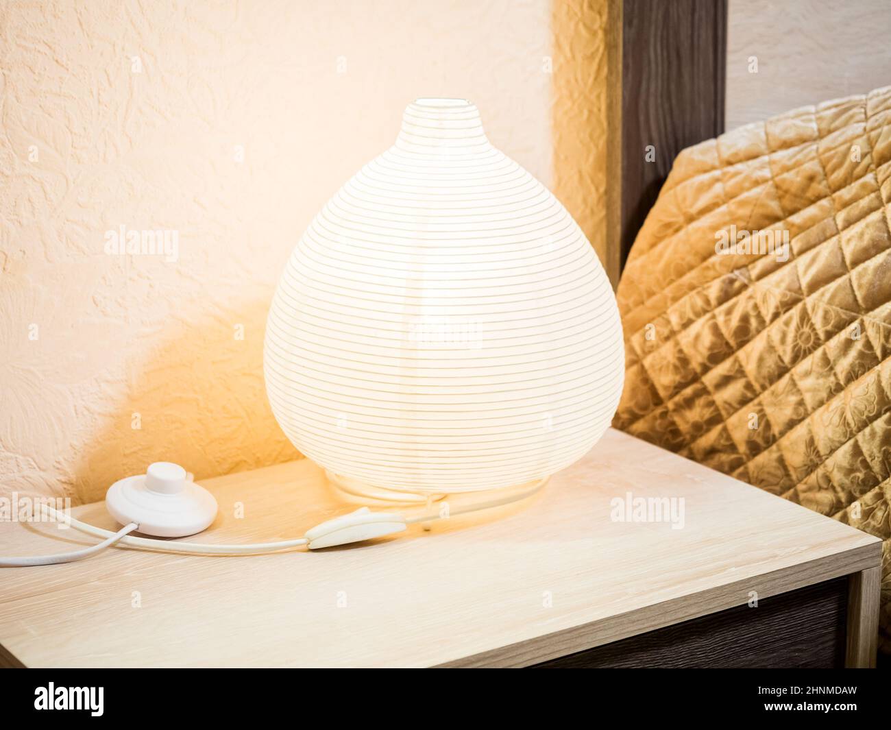 A luminous drop-shaped bedside lamp stands on light wooden bedside ...