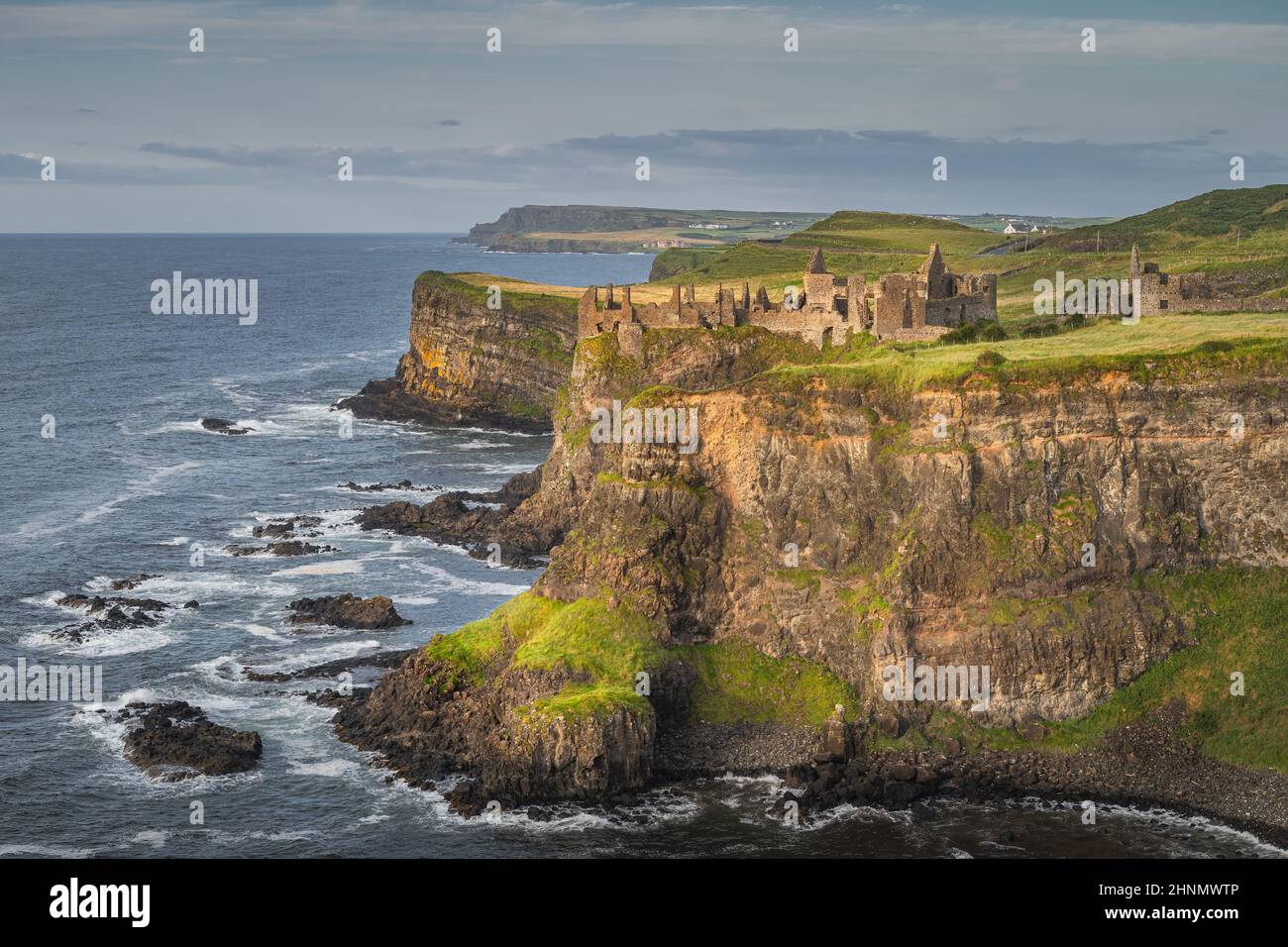 Dunluce Castle illuminated by sunlight, perched on the edge of cliff ...