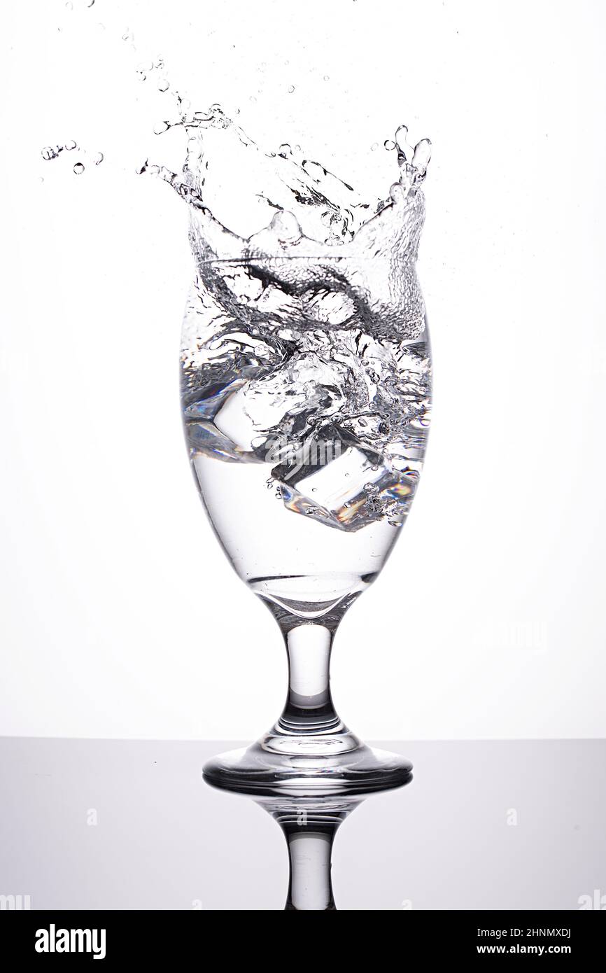 A studio photo of ice being dropped into a glass of water against a ...