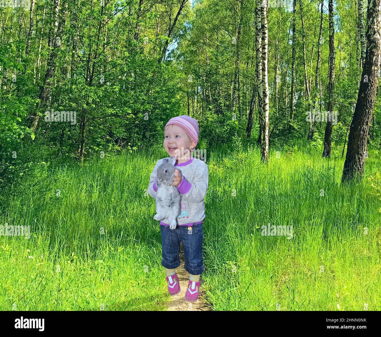 Girl with rabbit in arms standing on path in spring park. Happy child ...