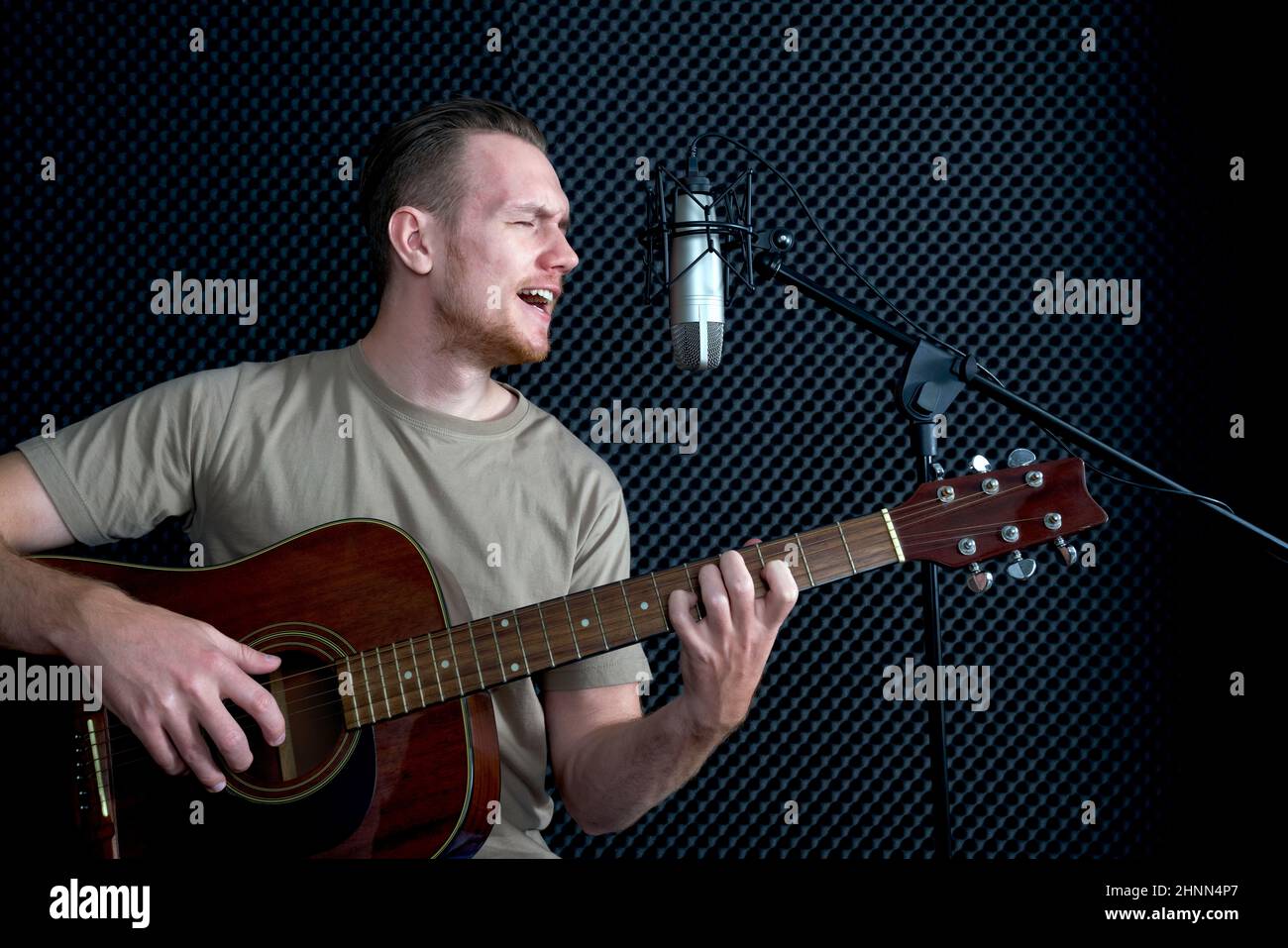 Young caucasian man sings while playing an acoustic guitar in front of ...