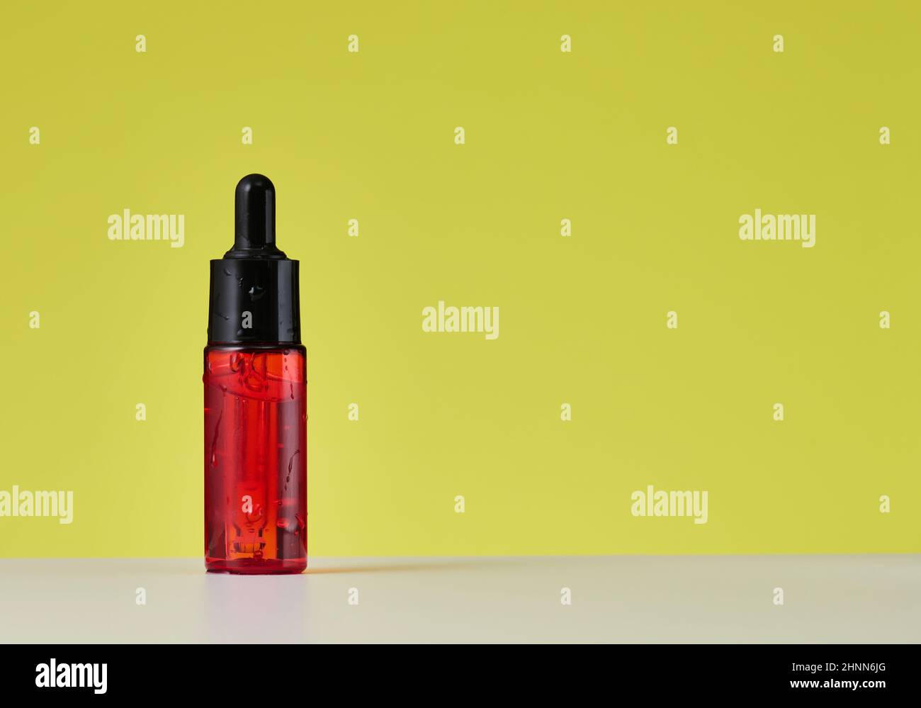 a glass transparent red bottle with a pipette stands on a white table ...