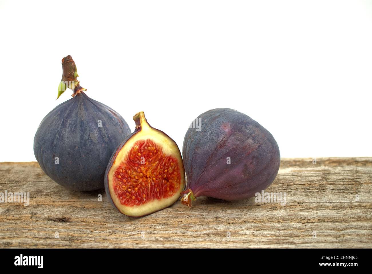 Ripe, purple figs on wooden table with sliced one fig over a white ...