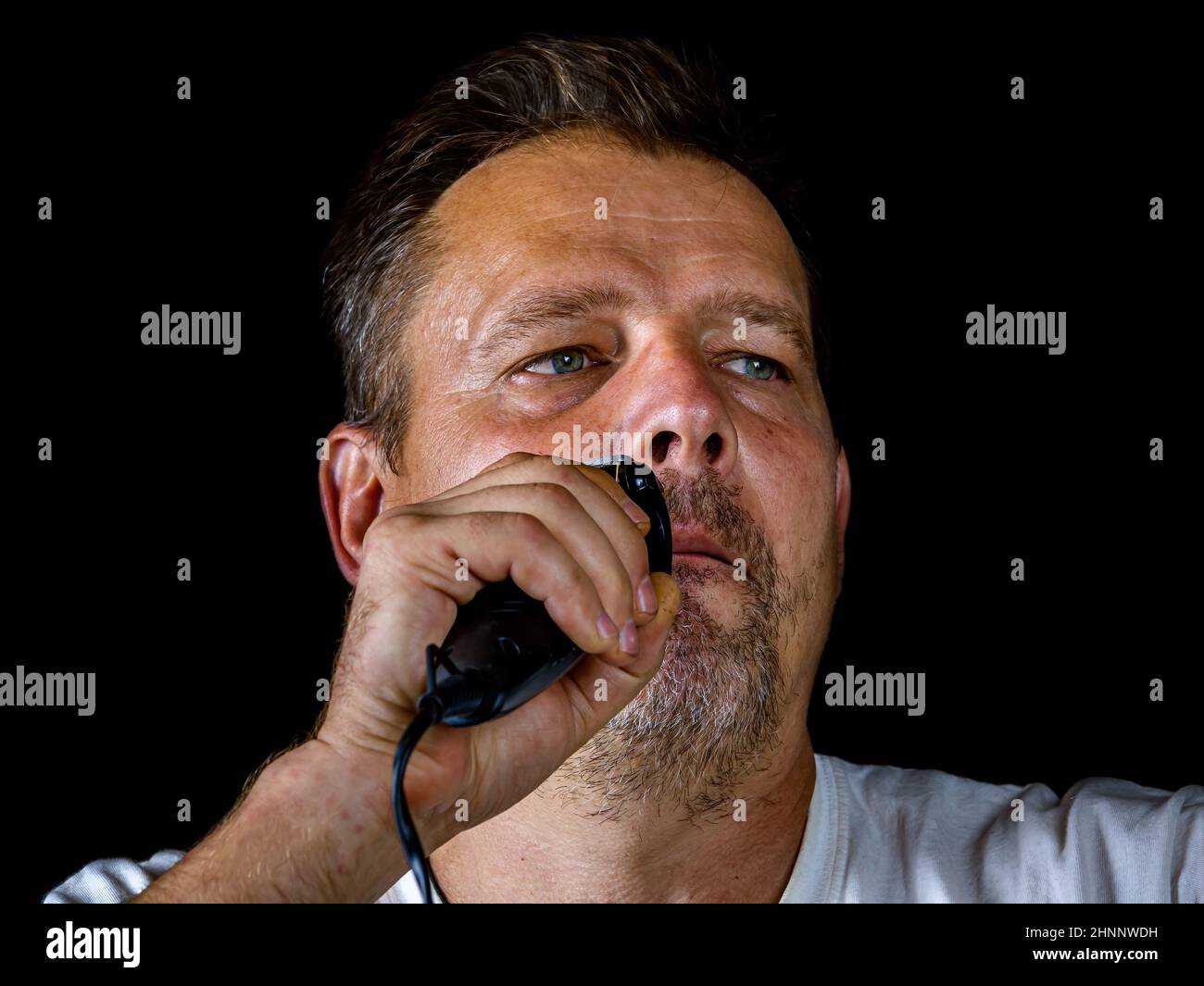 A middle-aged man cuts his gray beard with a shaving trimmer Stock ...