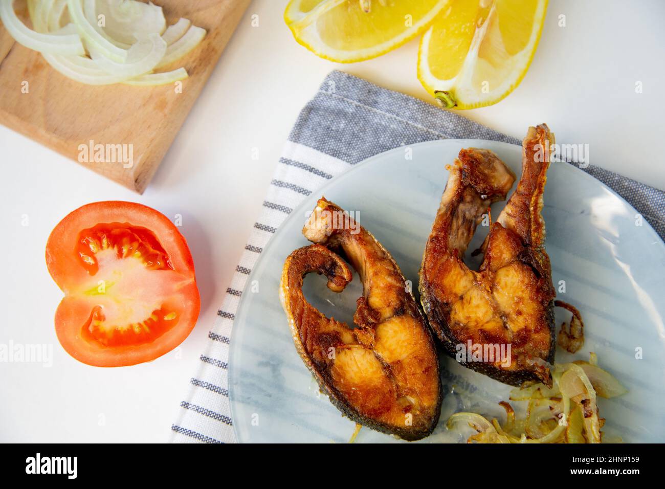Fried fish with onions is on a plate, on a waffle towel, next to it is ...