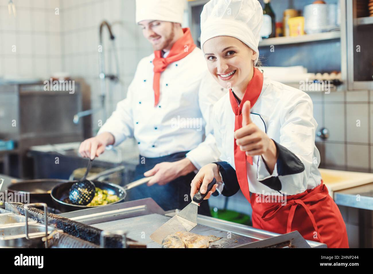 Chefs in restaurant kitchen cooking and giving the thumbs up as a sign ...