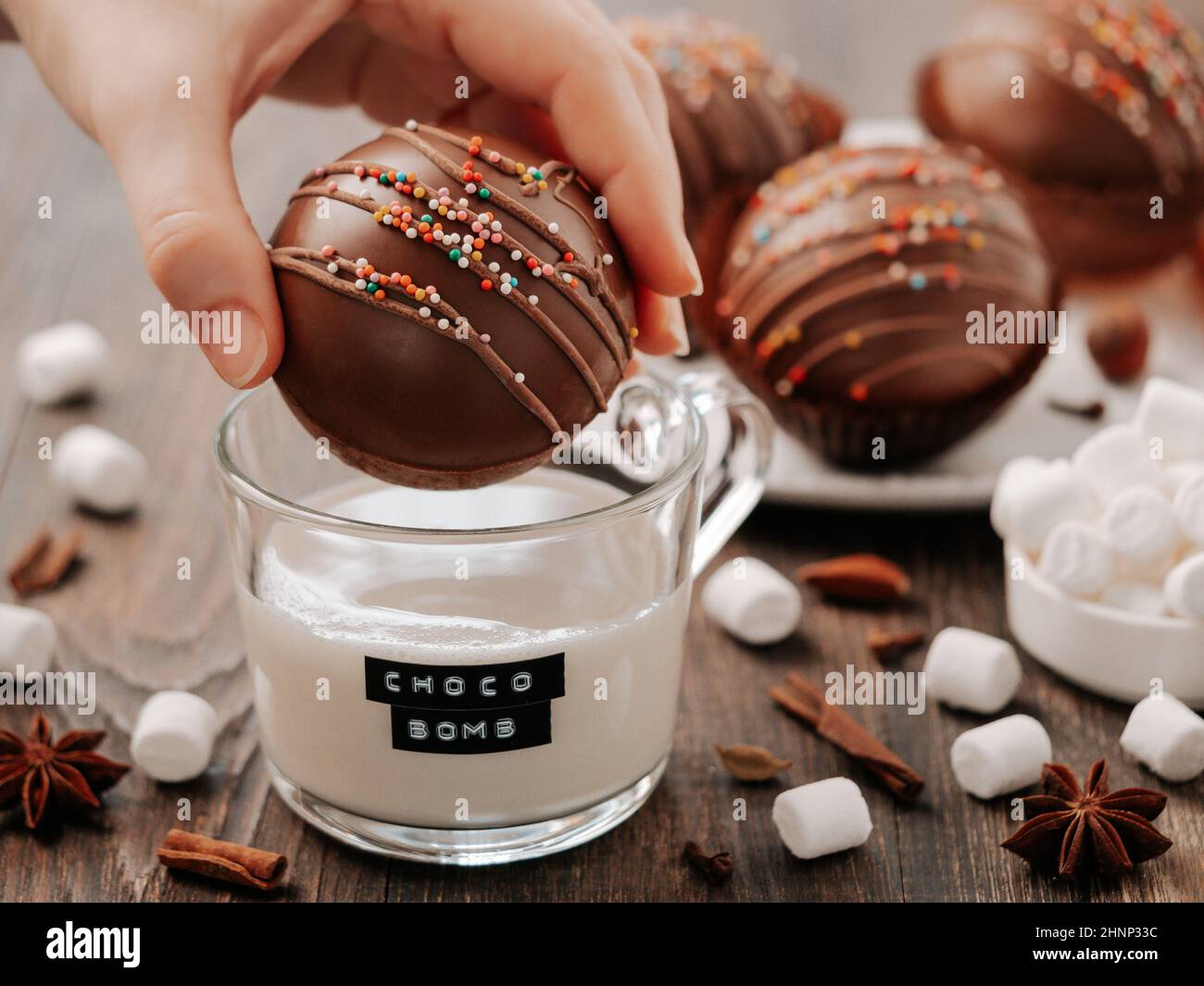 Chocolate cocoa bomb in hand near glass cup with plant-based milk and ...
