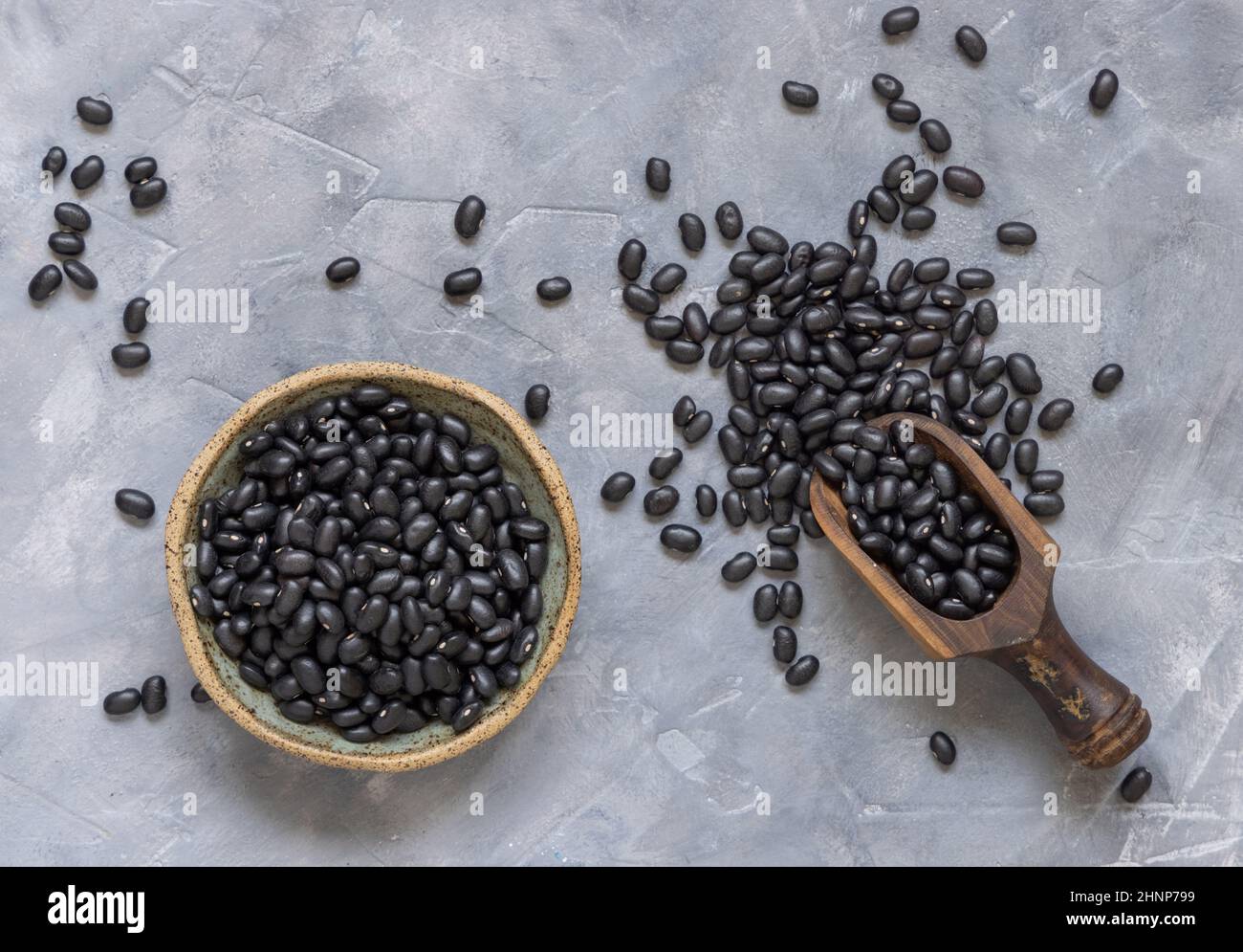 Bowl full of dried black beans with a wooden scoop on grey table top ...