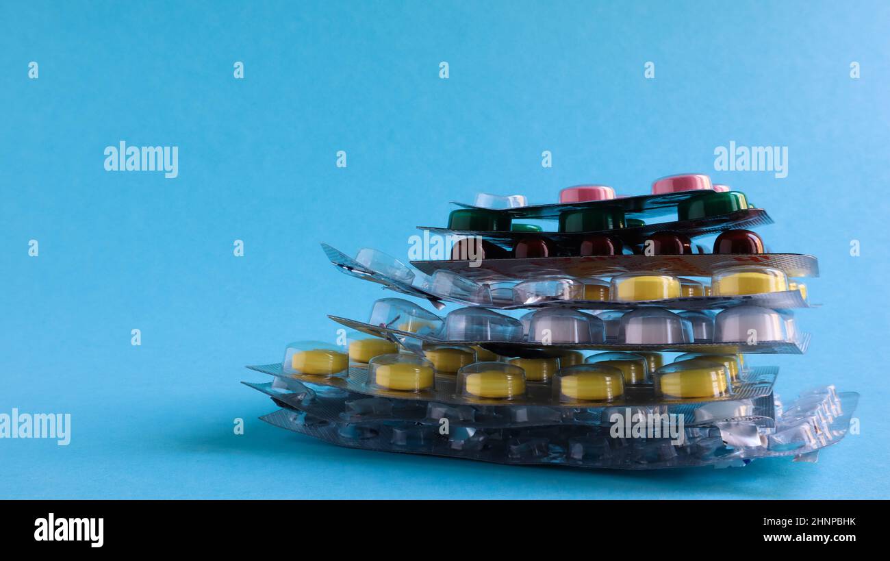 Packs of pills of various shapes and colors are stacked on a blue ...