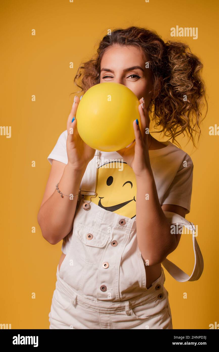 girl inflates a balloon on a yellow background .Young beautiful girl ...