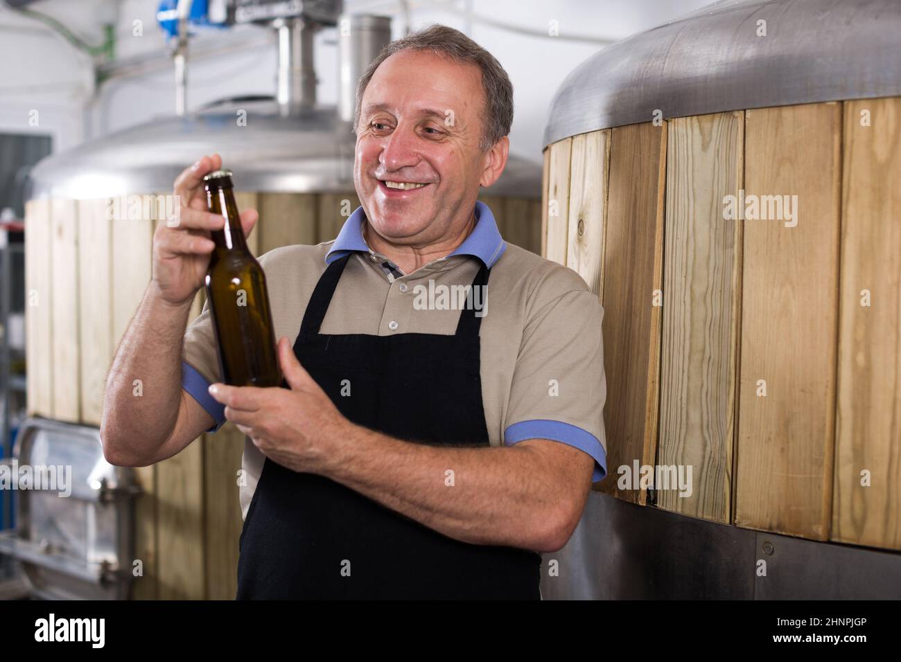 Brewer is standing with bottle for beer on his workplace Stock Photo ...
