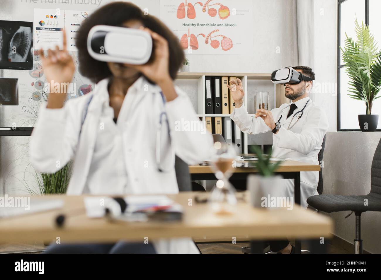 Two multicultural male and female doctors wearing VR goggles while ...