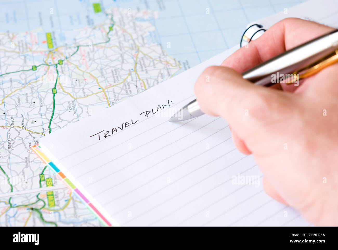 Hand writing travel plan in a lined spiral notepad arranged on a map ...