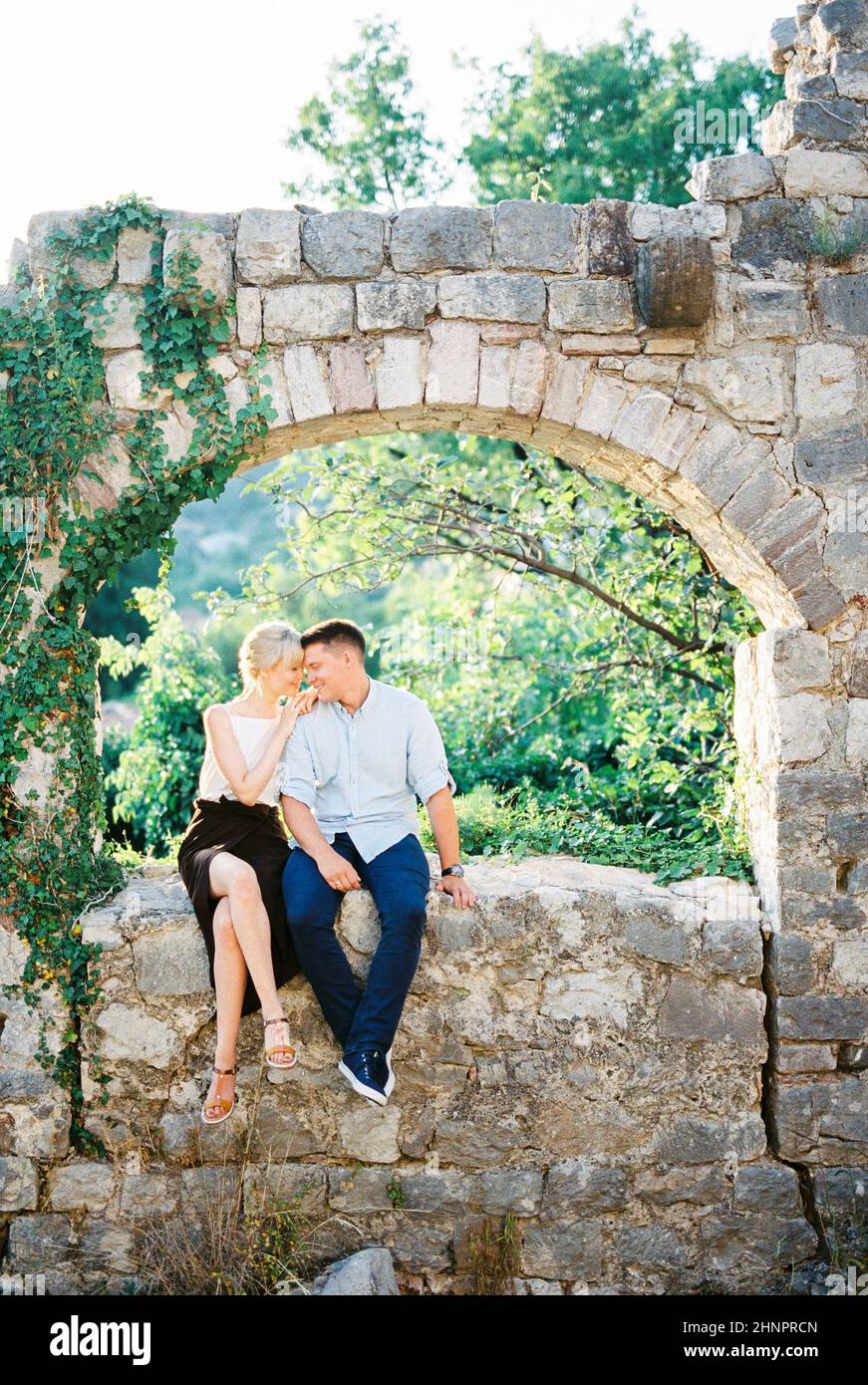 Man and woman sit hugging in a stone arch on the ruins of a castle ...