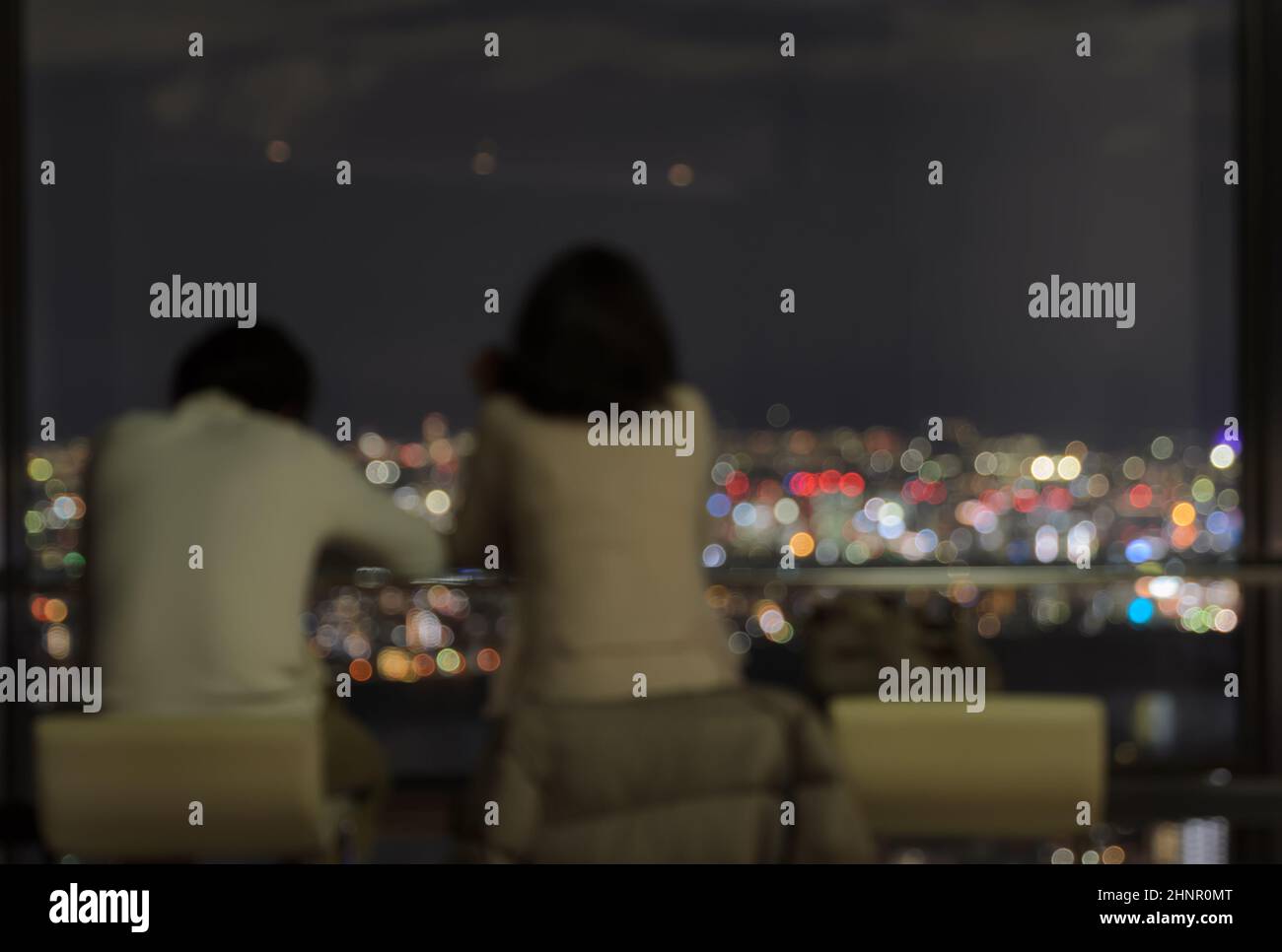 Blur couple sitting on skyscraper observatory overlooking the night ...