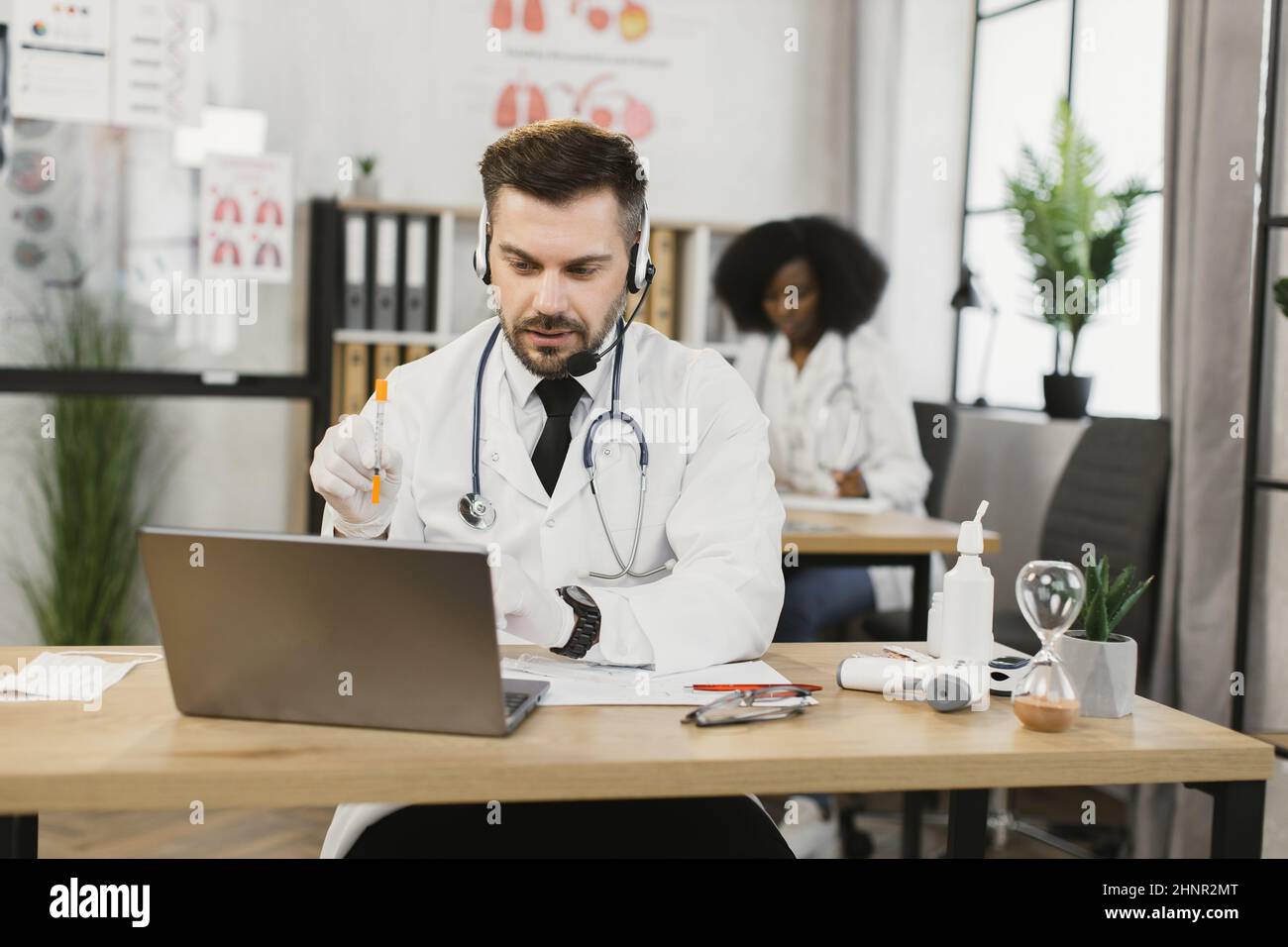 Confident caucasian doctor in white lab coat and gloves using headset ...