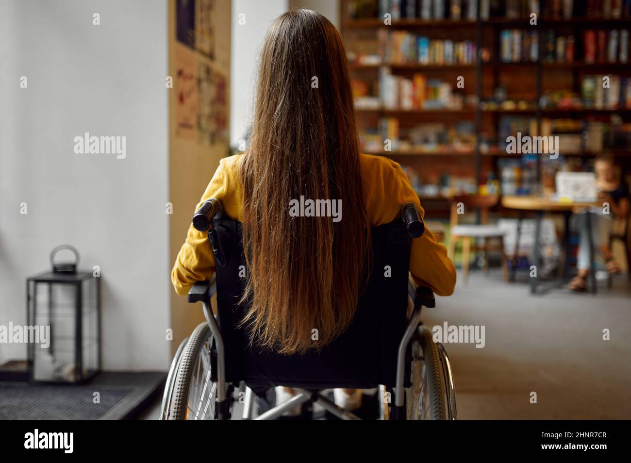 Disabled female student in wheelchair, back view, disability, bookshelf ...