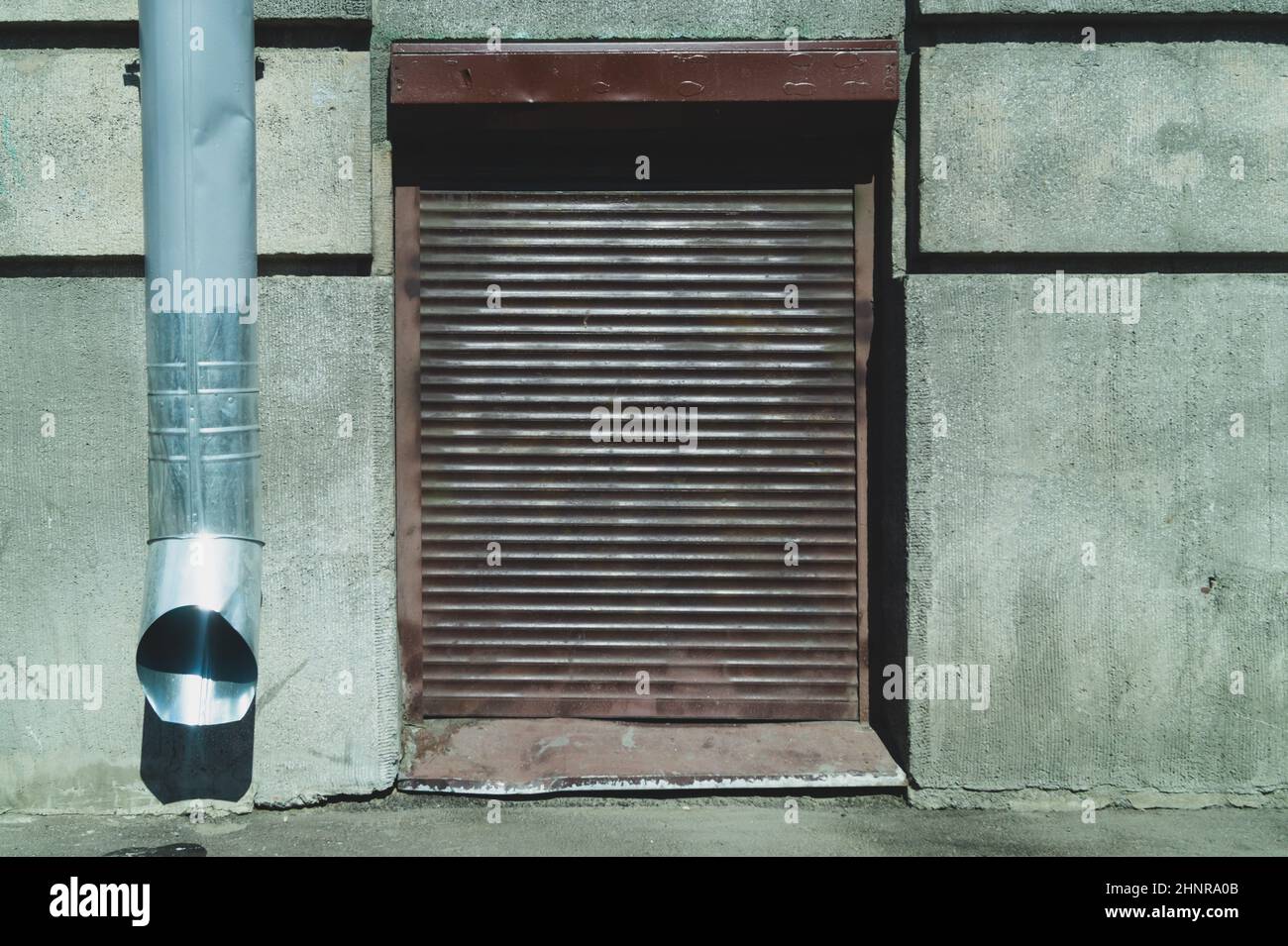 Corrugated iron blind on a concrete wall. drain pipe. metal curtain ...
