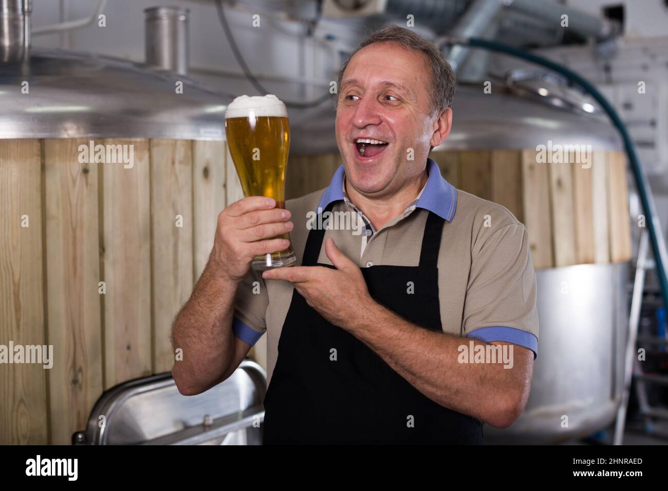Portrait of brewer who is standing with glass of beer on his workplace ...