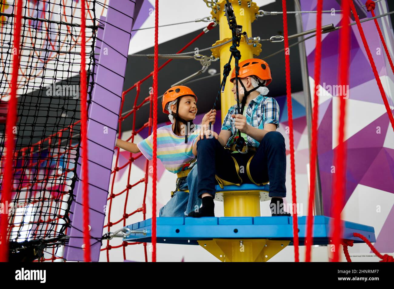 Two children in helmets climb on tightropes in entertainment center ...