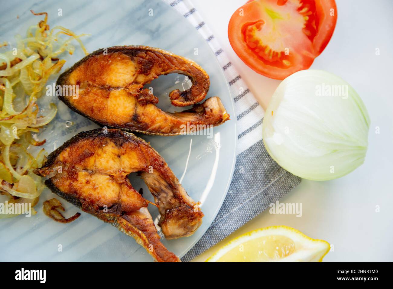 Fried fish with onions lies on a plate, on a waffle towel, next to a ...