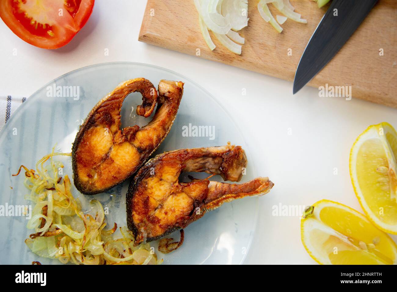 Fried fish with onions is on a plate, on a waffle towel, next to it is ...