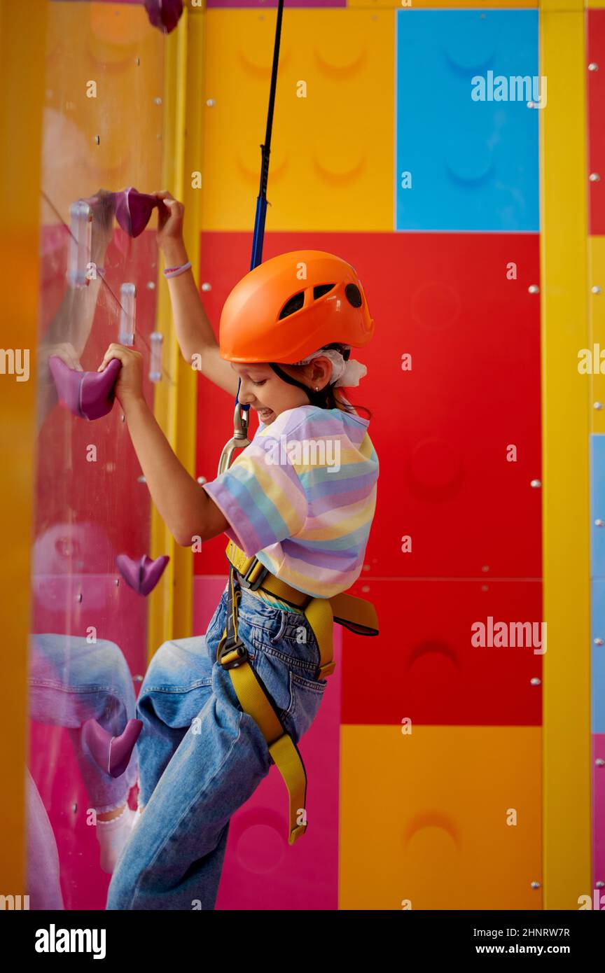 Little girl in helmet poses on climbing wall, entertainment center ...