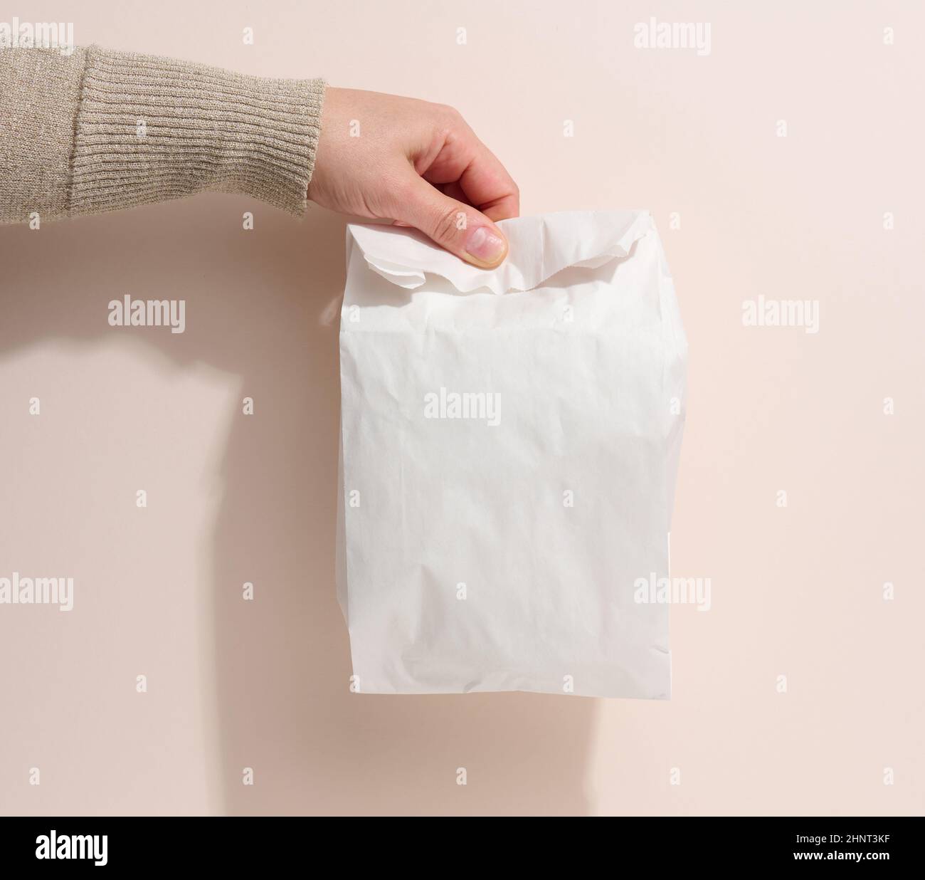 female hand holds a full paper bag on a beige background. Refusal from ...