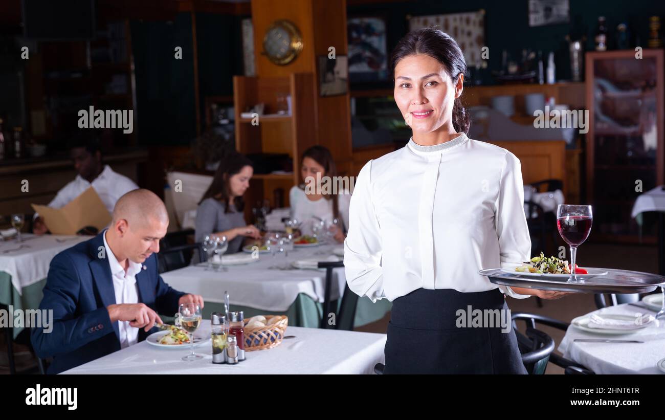 Polite waitress with serving tray warmly welcoming in restaurant Stock ...