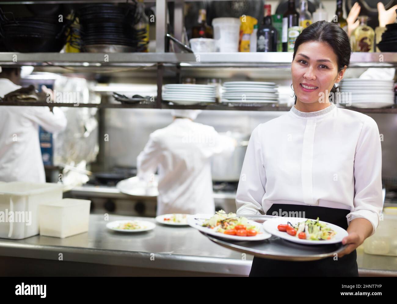 portrait of smiling female waiter standing in kitchen in restaurante ...