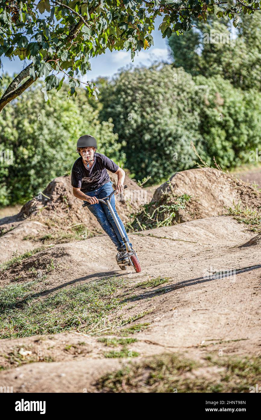 boy rides his push scooter in a bike park with ramps of loam Stock ...