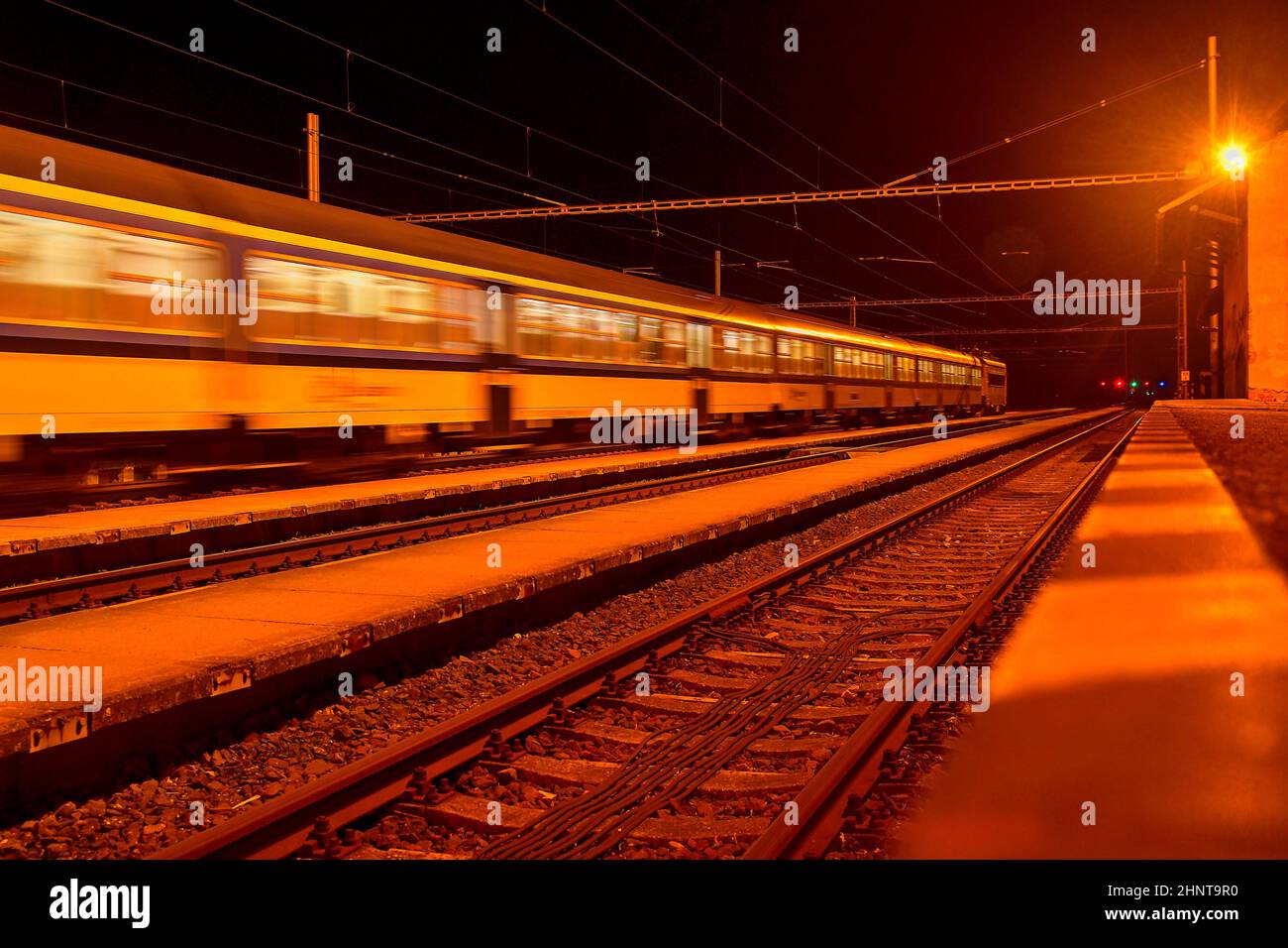 White and blue train passing a small roofless train station at night in ...