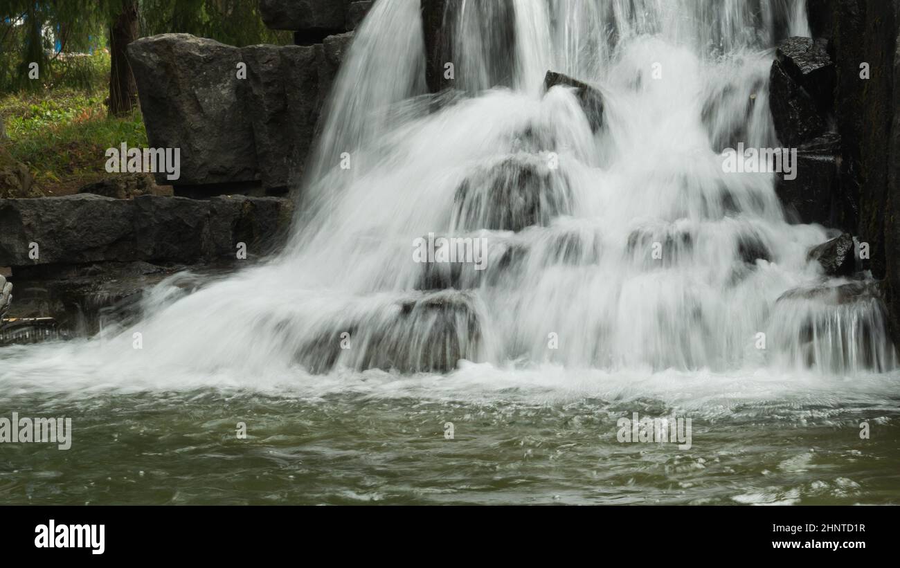 Small waterfall flows into a pond. rushing stream water background ...